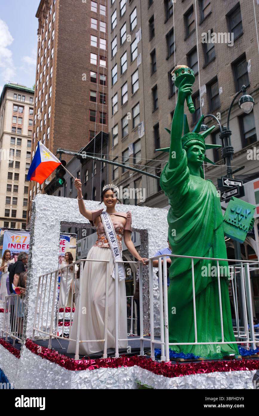 A pageant winner in a long white gown stands on a float, holding a ...