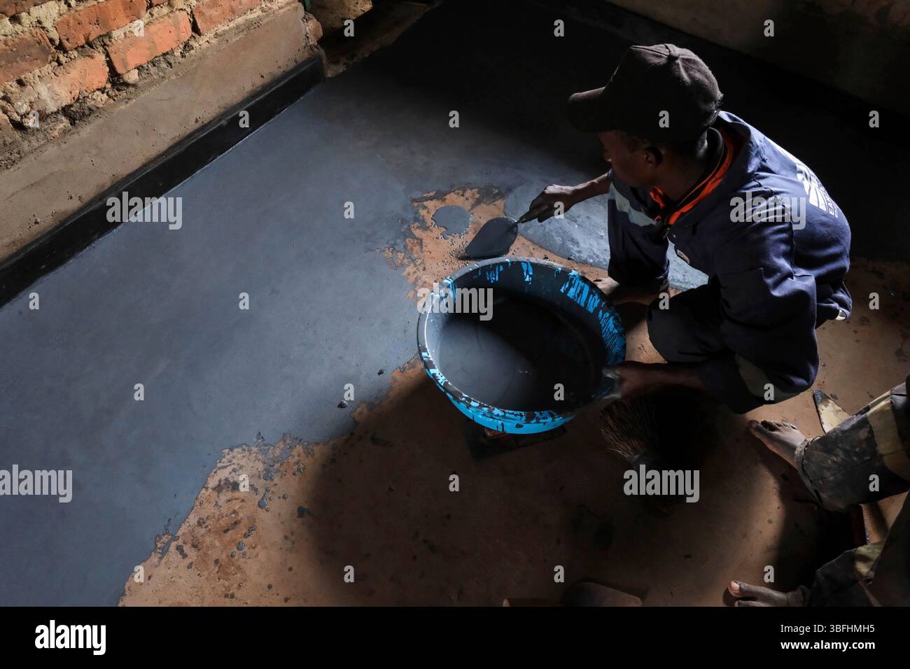 Alex Wanda, a construction officer at EarthEnable, installs paste on floors May 17, 2025, in ...