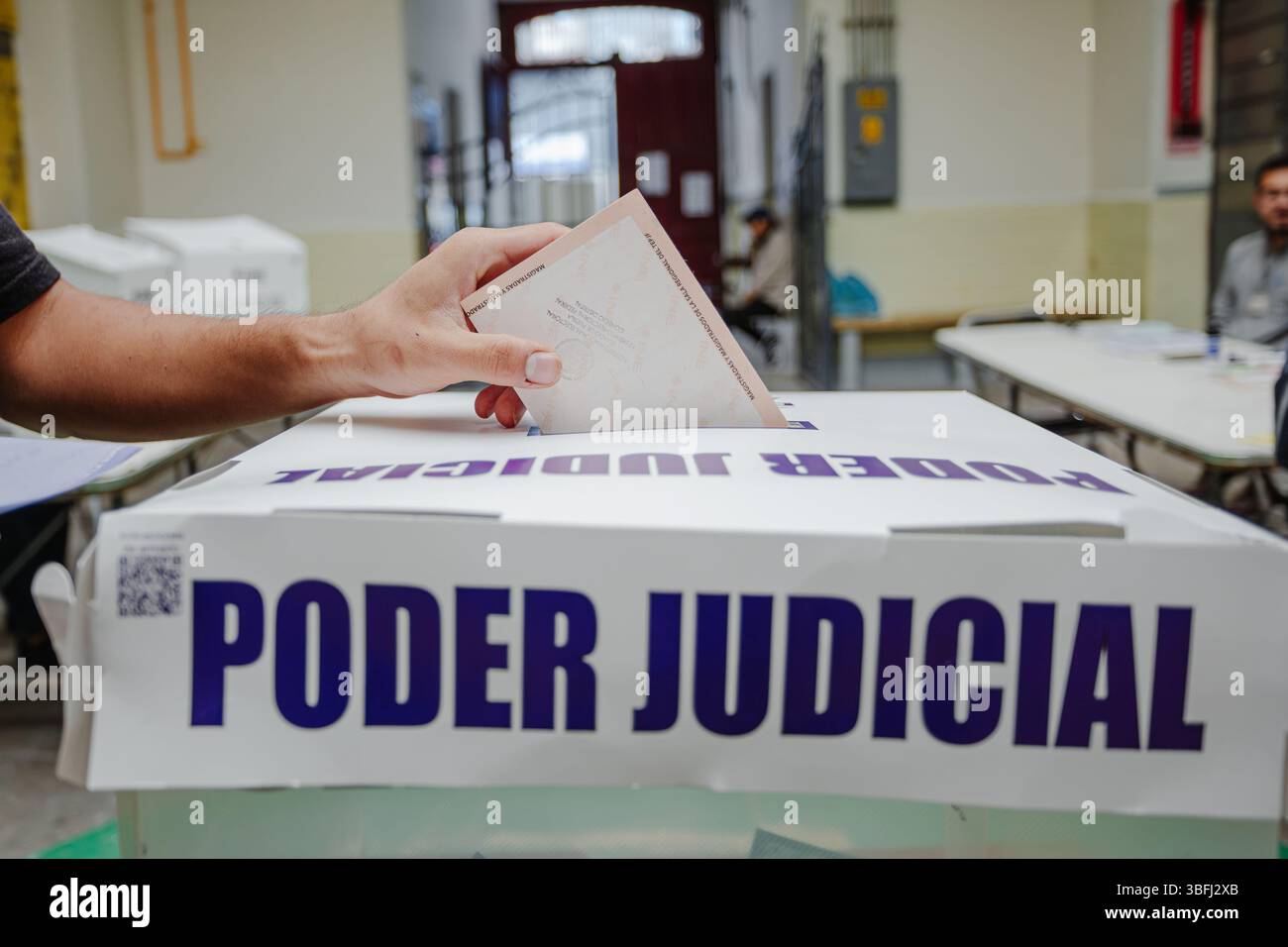 A hand places a ballot into a transparent box labeled “Poder Judicial ...