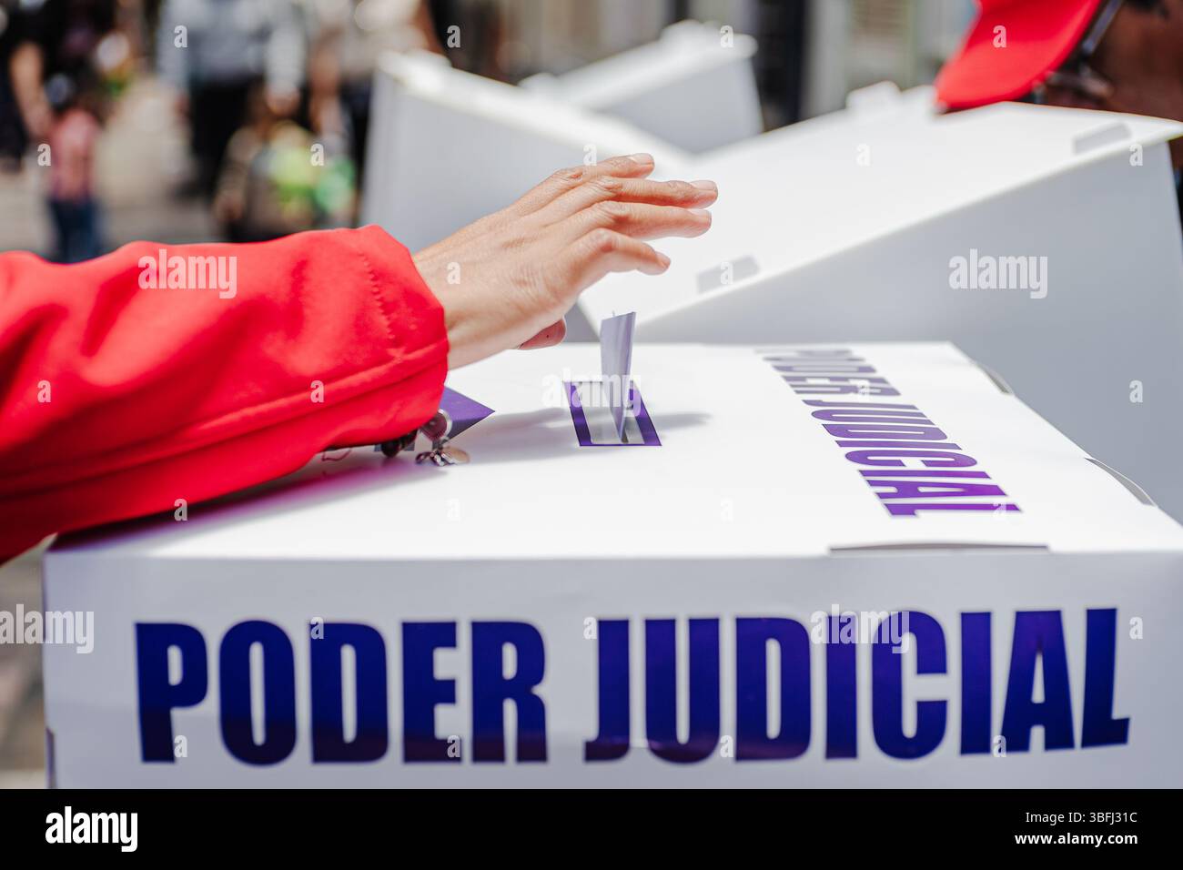 A hand places a ballot into a transparent box labeled “Poder Judicial ...