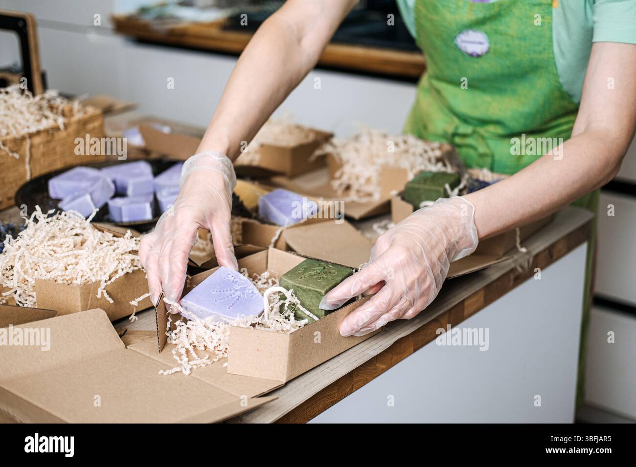 Person arranges lavender and olive oil soaps into kraft boxes with shredded filler at a ...