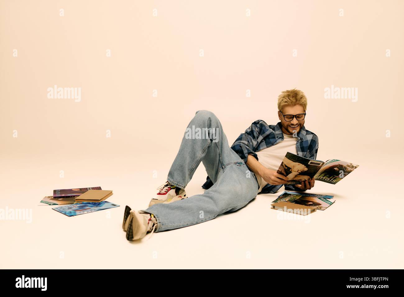 Smiling young man relaxes on the floor, reading graphic novels with ...