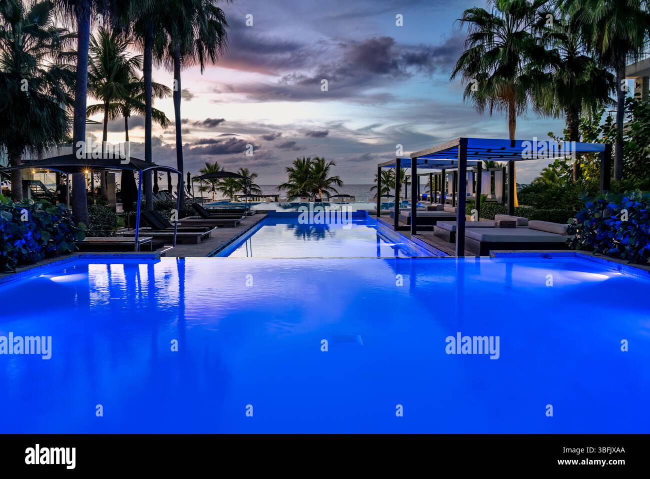 Blue lit infinity pool at sunset at a beach resort Stock Photo - Alamy