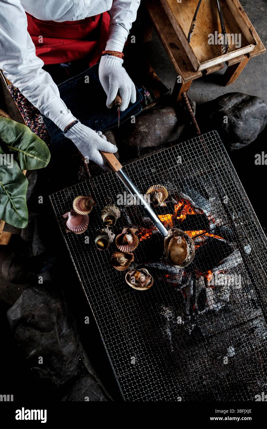 Japanese Ama diver cooks shellfish on grill in traditional Ama hut ...