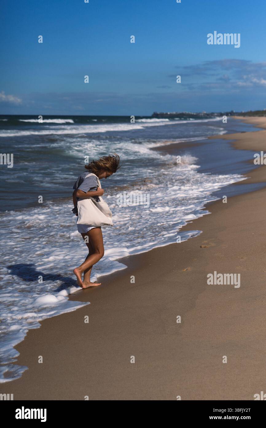 Woman running barefoot by ocean waves on sunny beach Stock Photo - Alamy