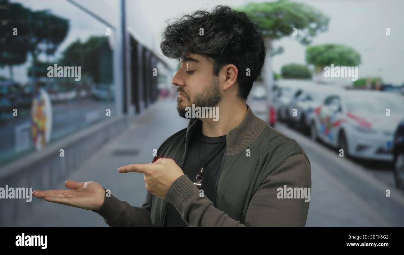 Young hispanic man with beard pointing to palm outdoors on a street ...