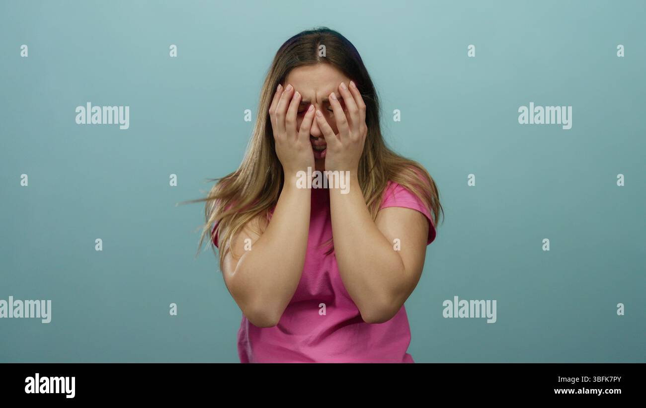 Woman distressed, hands on face over blue background, expressing ...
