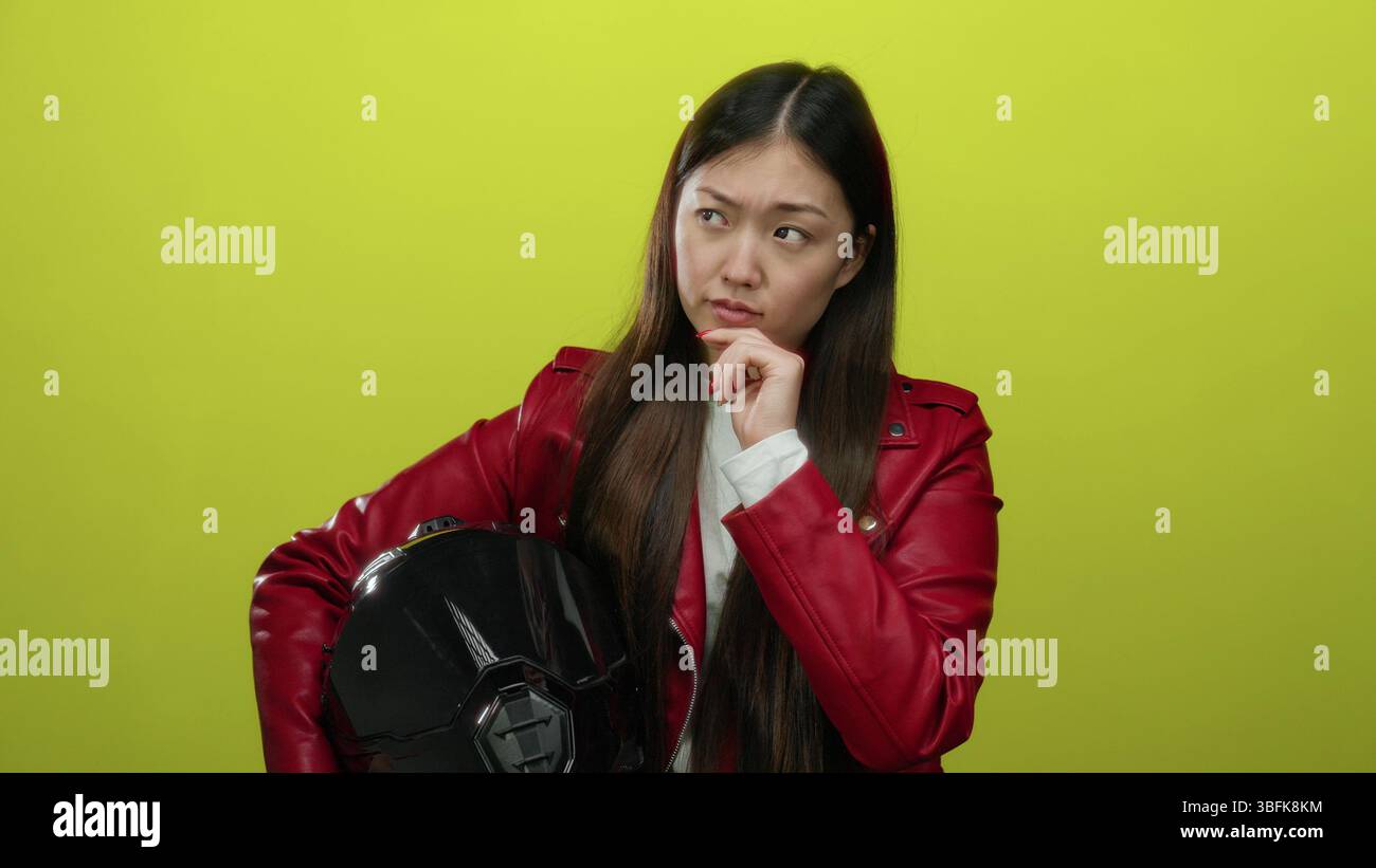 Woman pondering holding helmet in red jacket against vibrant yellow ...