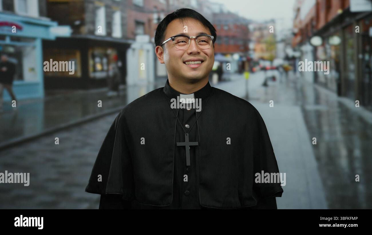Smiling priest wearing glasses standing on an urban street outside in a ...