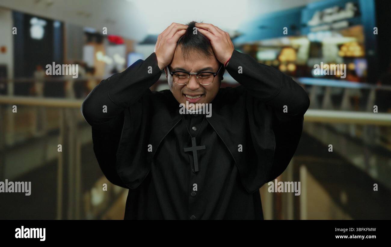 Priest wearing black robe and glasses in a mall expresses stress while ...