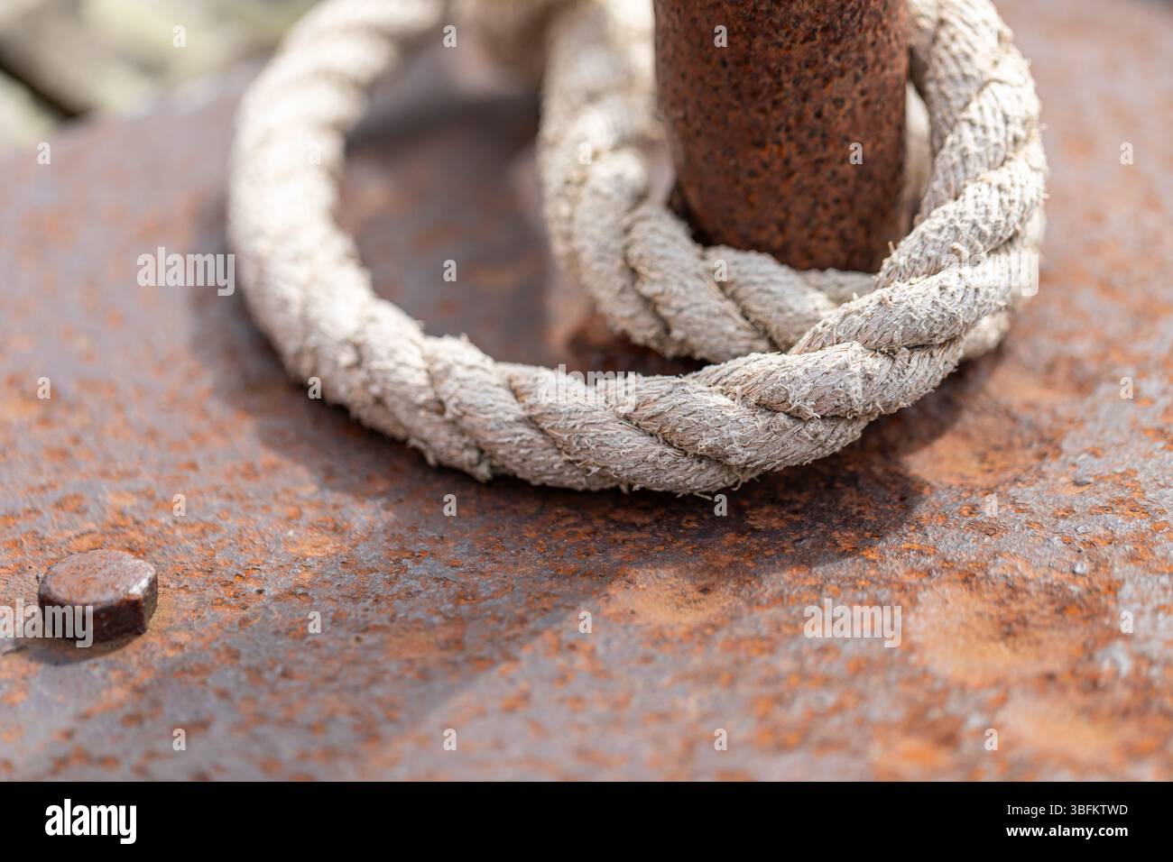 Close-up of sun-bleached rope wrapped around rusty metal bollard. The ...