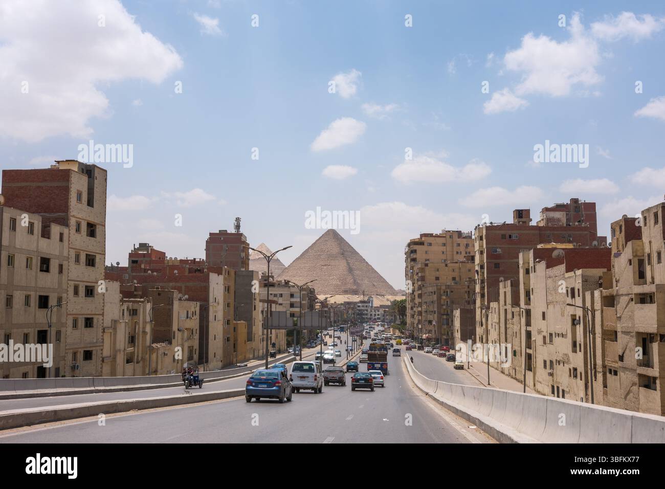 Cars passing by buildings with the Great Pyramid of Giza in the ...