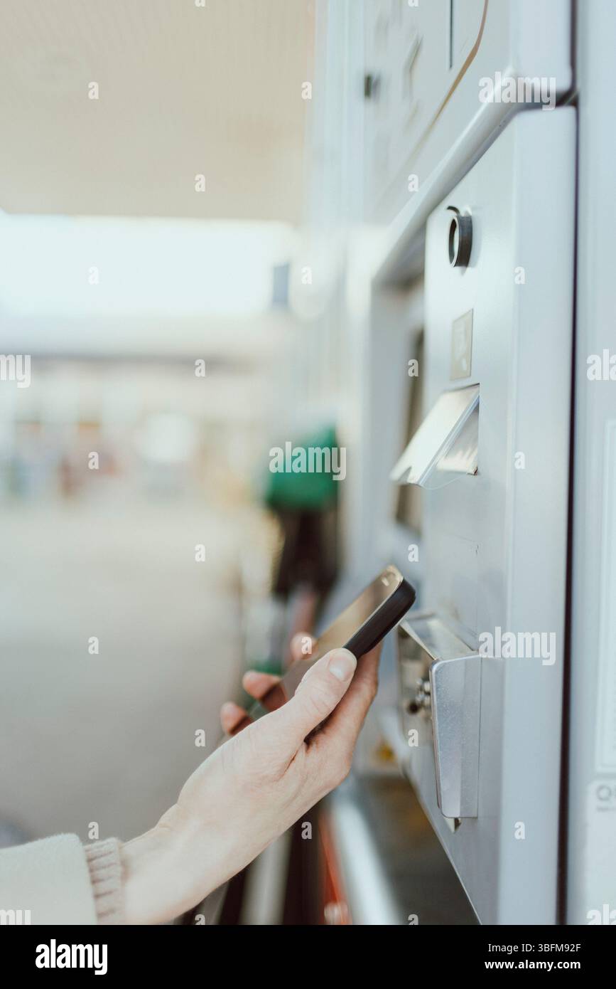 Hand of woman scanning QR code through smart phone at gas station kiosk ...