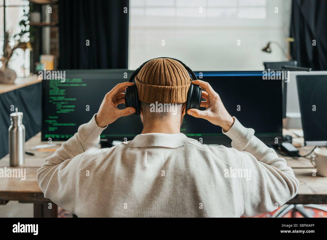 Rear view of male computer programmer wearing wireless headphones at ...