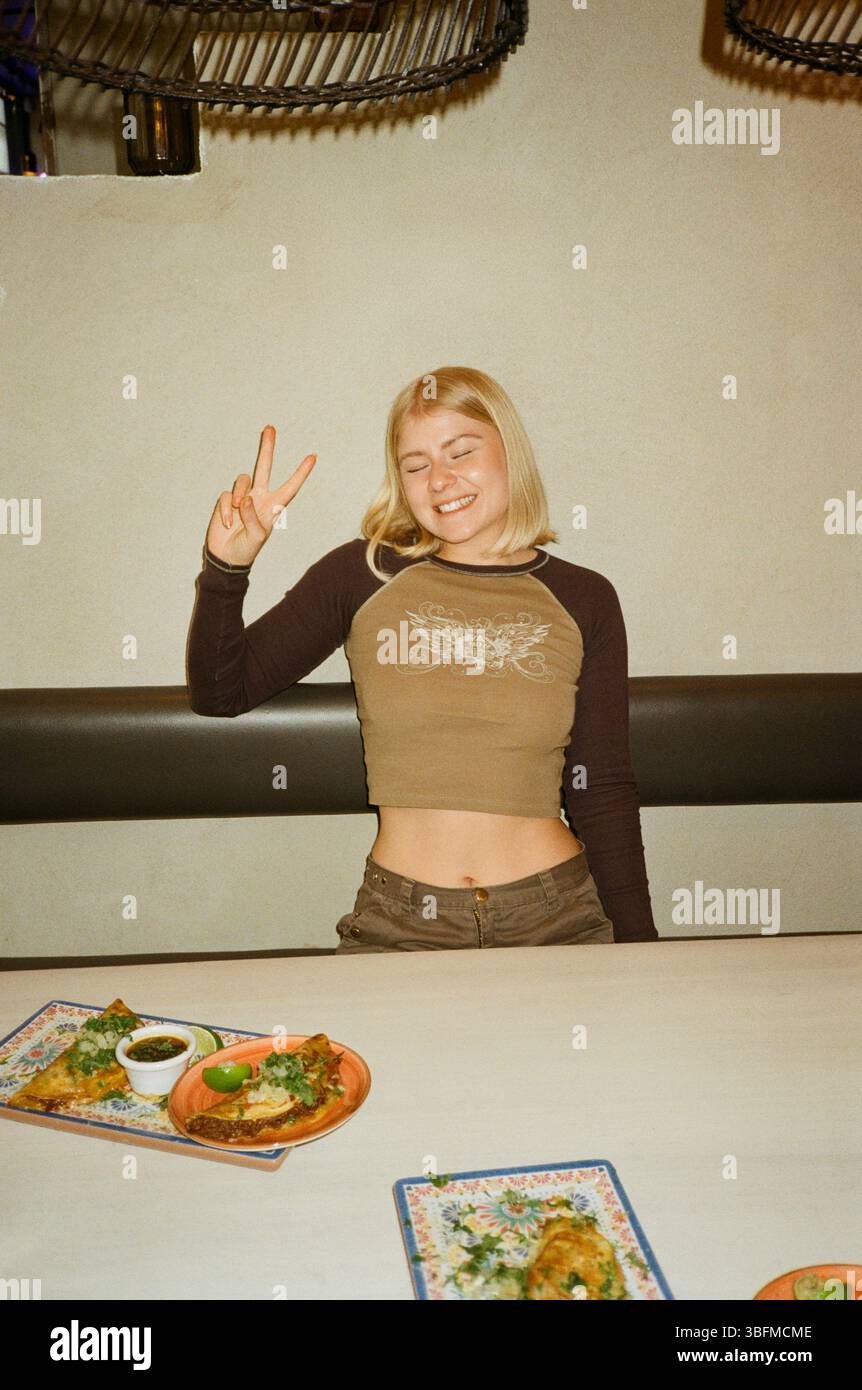 Smiling young woman showing peace sign while at fast food restaurant ...