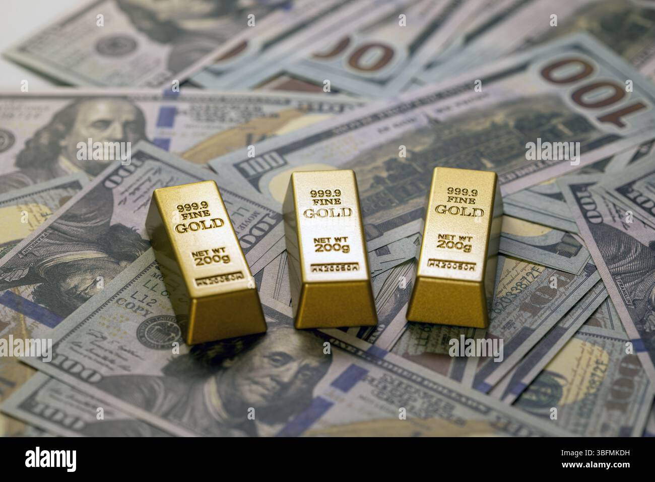 A three gold bars rest on spread of hundred dollar bills, symbolizing wealth and investment ...