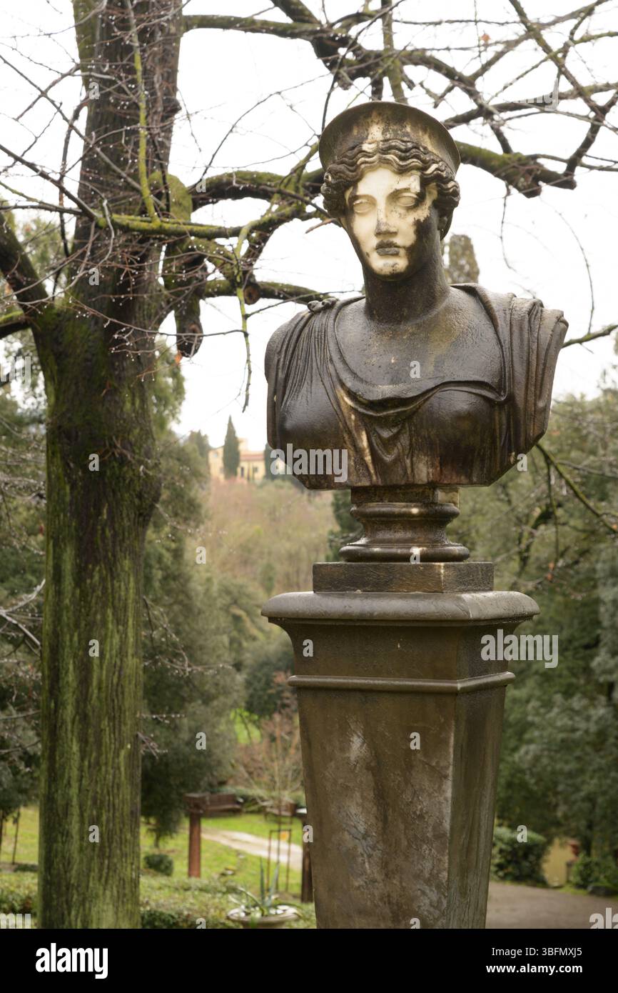 Weathered classical bust on a stone pedestal amid lush greenery in ...