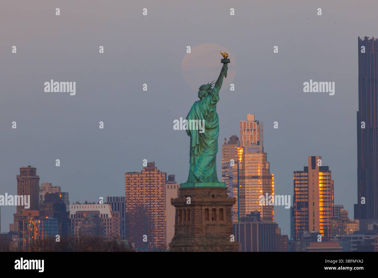 The Statue of Liberty raises her torch as the full moon rises behind it ...