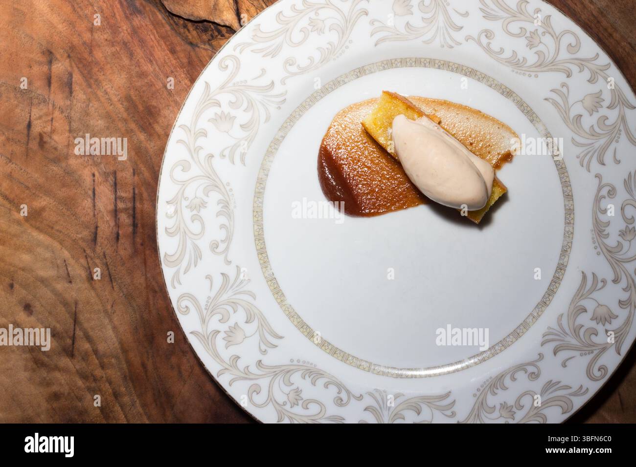 A chef plates a dessert with cake, sauce, and ice cream on a decorative ...