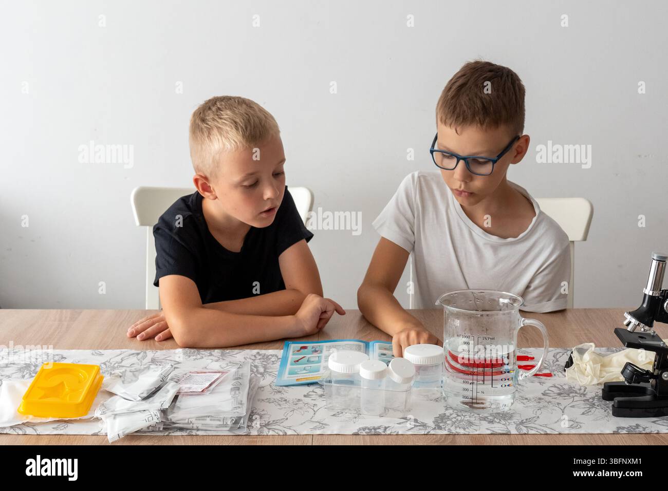 Two curious school boys doing science experiment at home with measuring cup, microscope, and ...