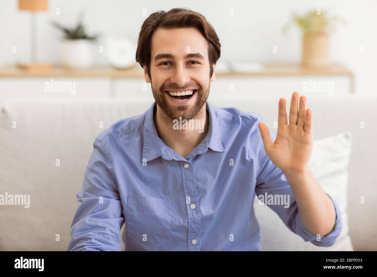 Happy Man Waving Hand To Camera Sitting At Home Stock Photo - Alamy