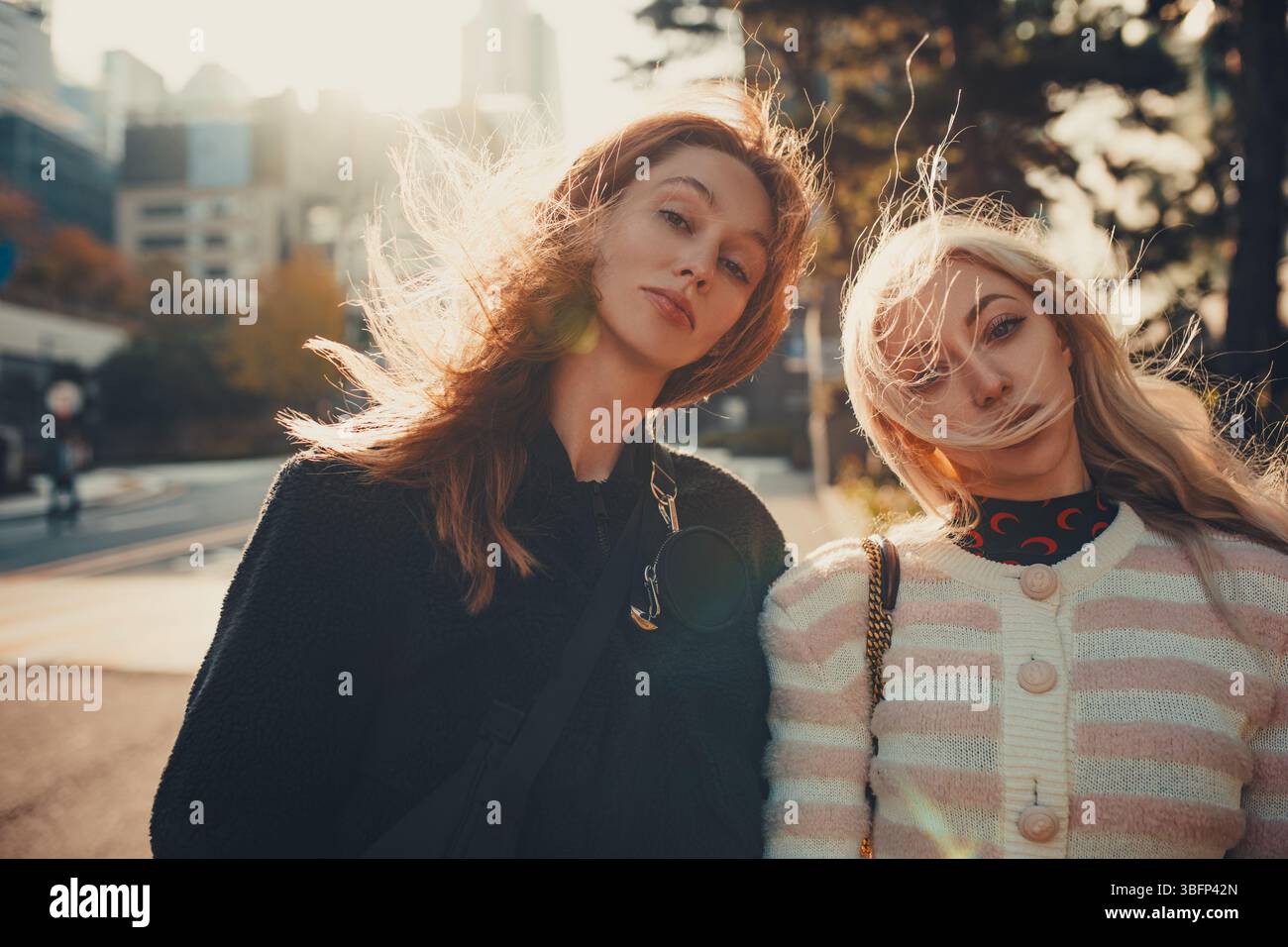 Two young women friends portrait on city street in windy day, summer ...