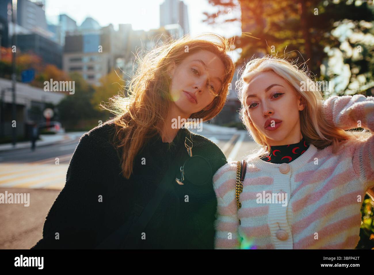 Two young women friends portrait on city street in windy day, summer ...
