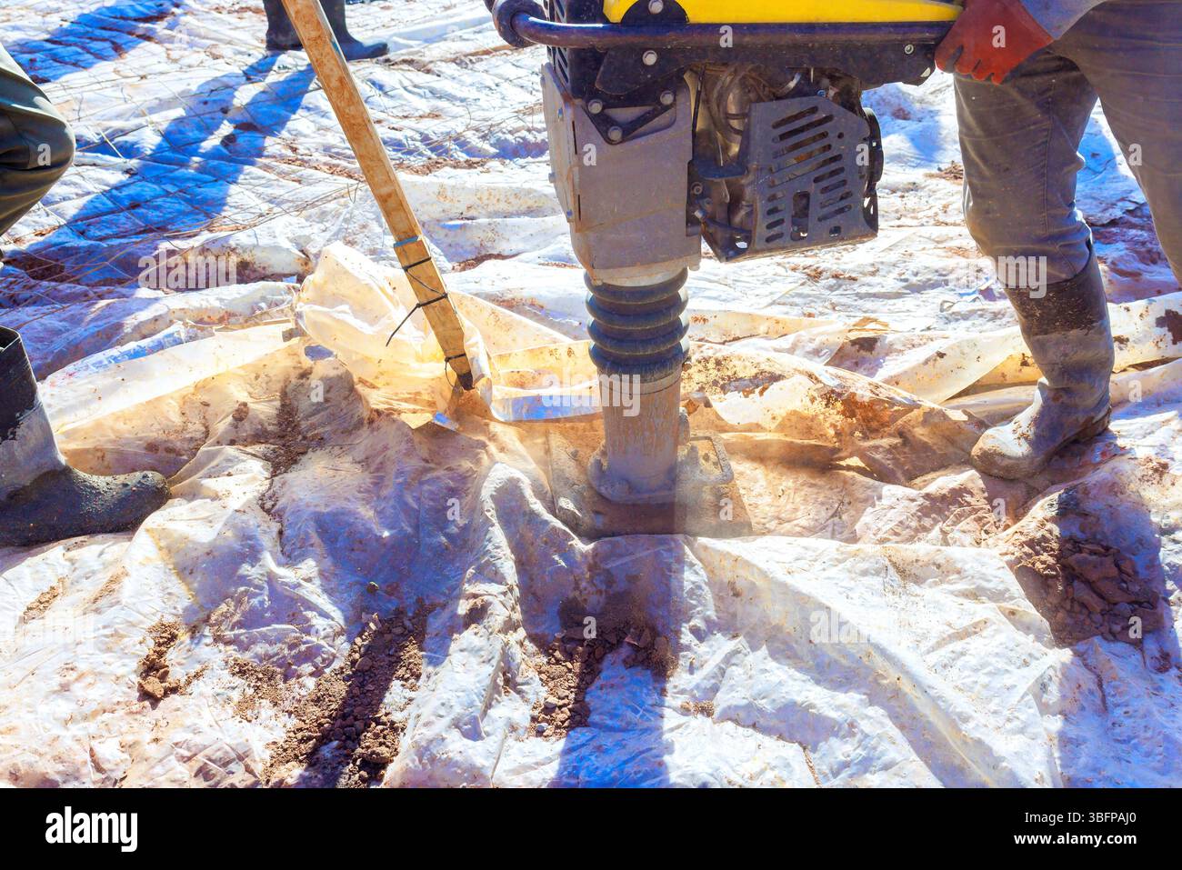 Construction workers use compactor to pack down soil on construction ...