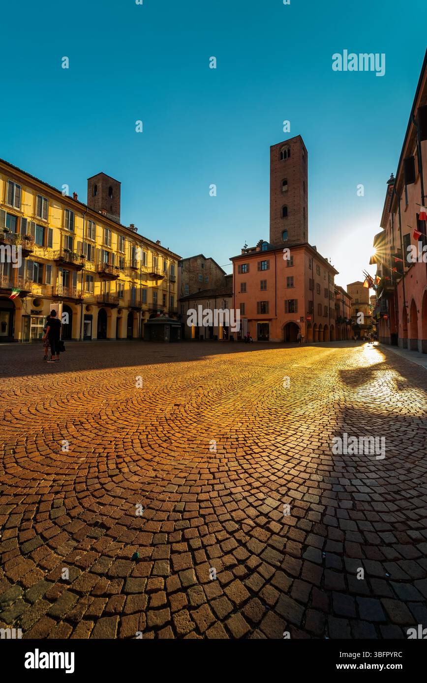 Sunlight illuminates a cobblestone town square with medieval towers and ...