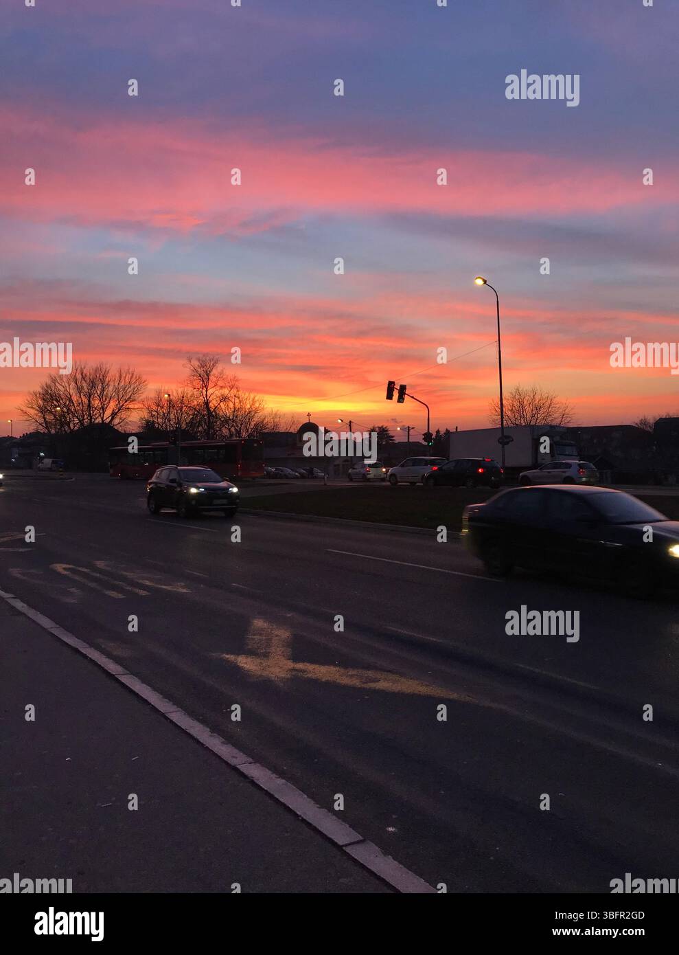 Urban traffic scene at dusk with colorful sunset sky and silhouettes of ...