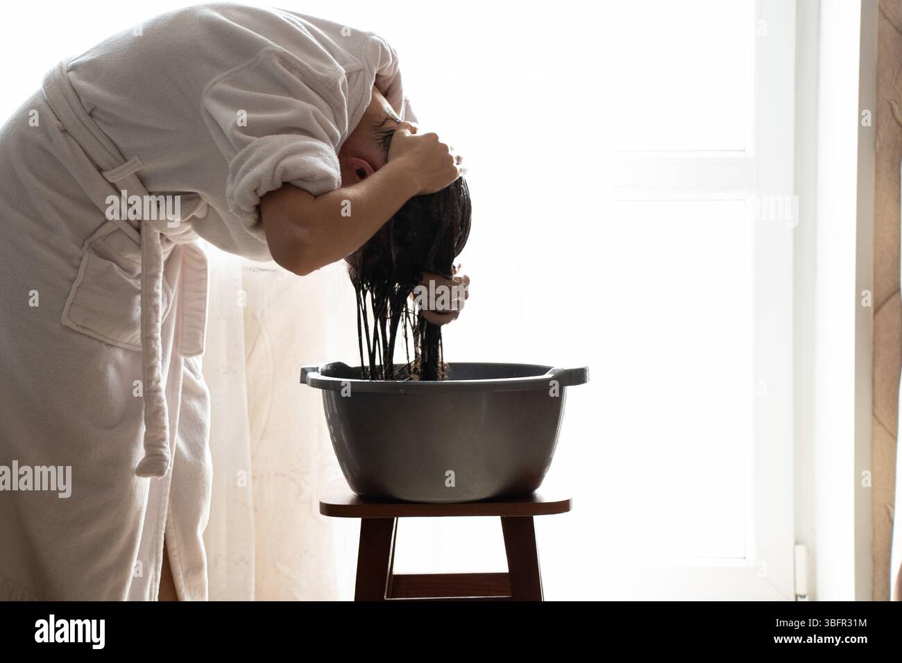 Girl washes hair in a basin at home, self-care at home without a shower ...