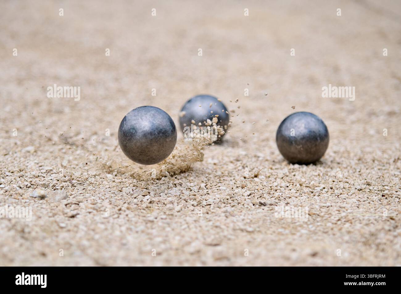 Flying petanque ball hits the ground, sending gravel into the air ...