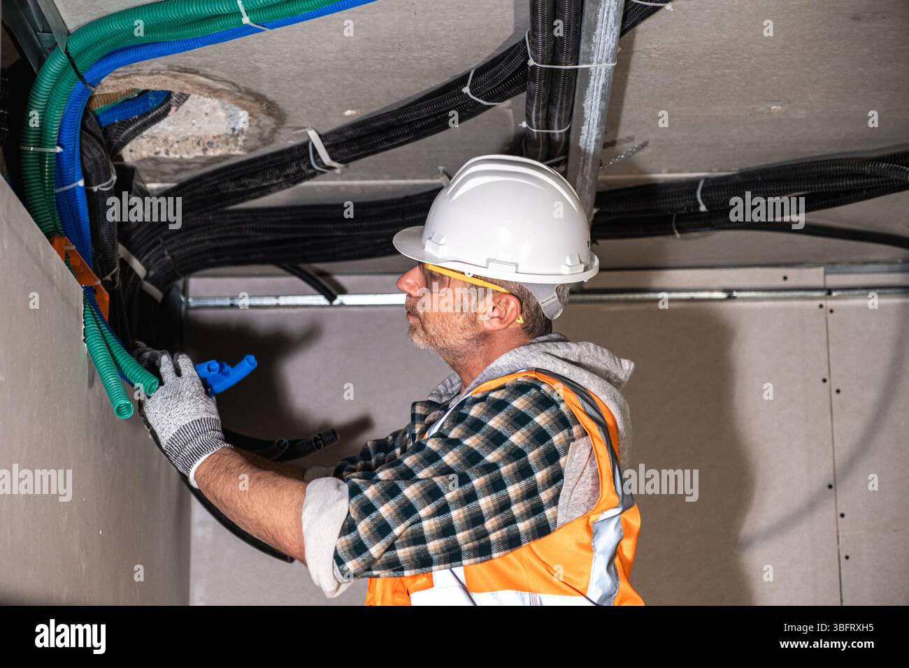 Electrician wearing safety gear adjusts green electrical conduit at ...
