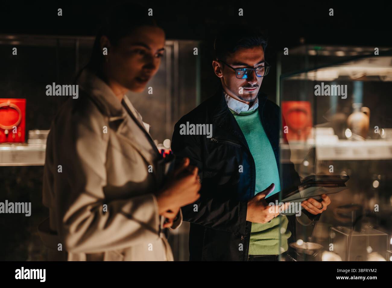 Two people observing an exhibit in a dimly lit museum showcasing ...