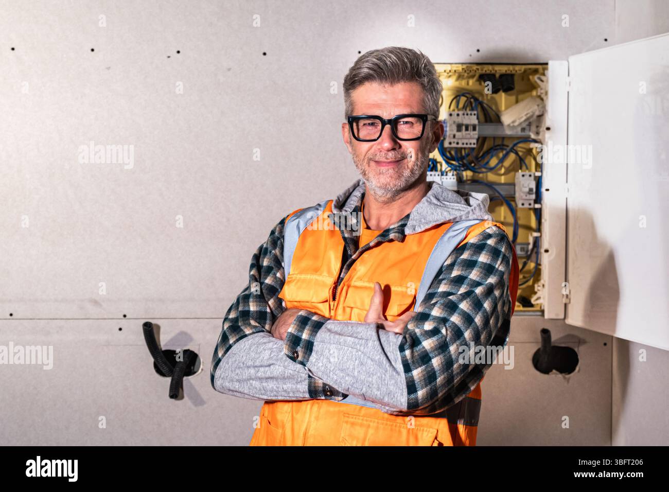 Smiling mature electrician in safety vest standing confidently with ...
