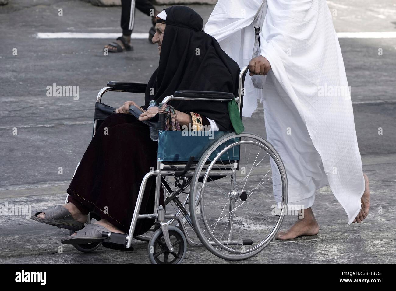 An Afghani elderly pilgrim on a wheel chair is pushed by her son ...