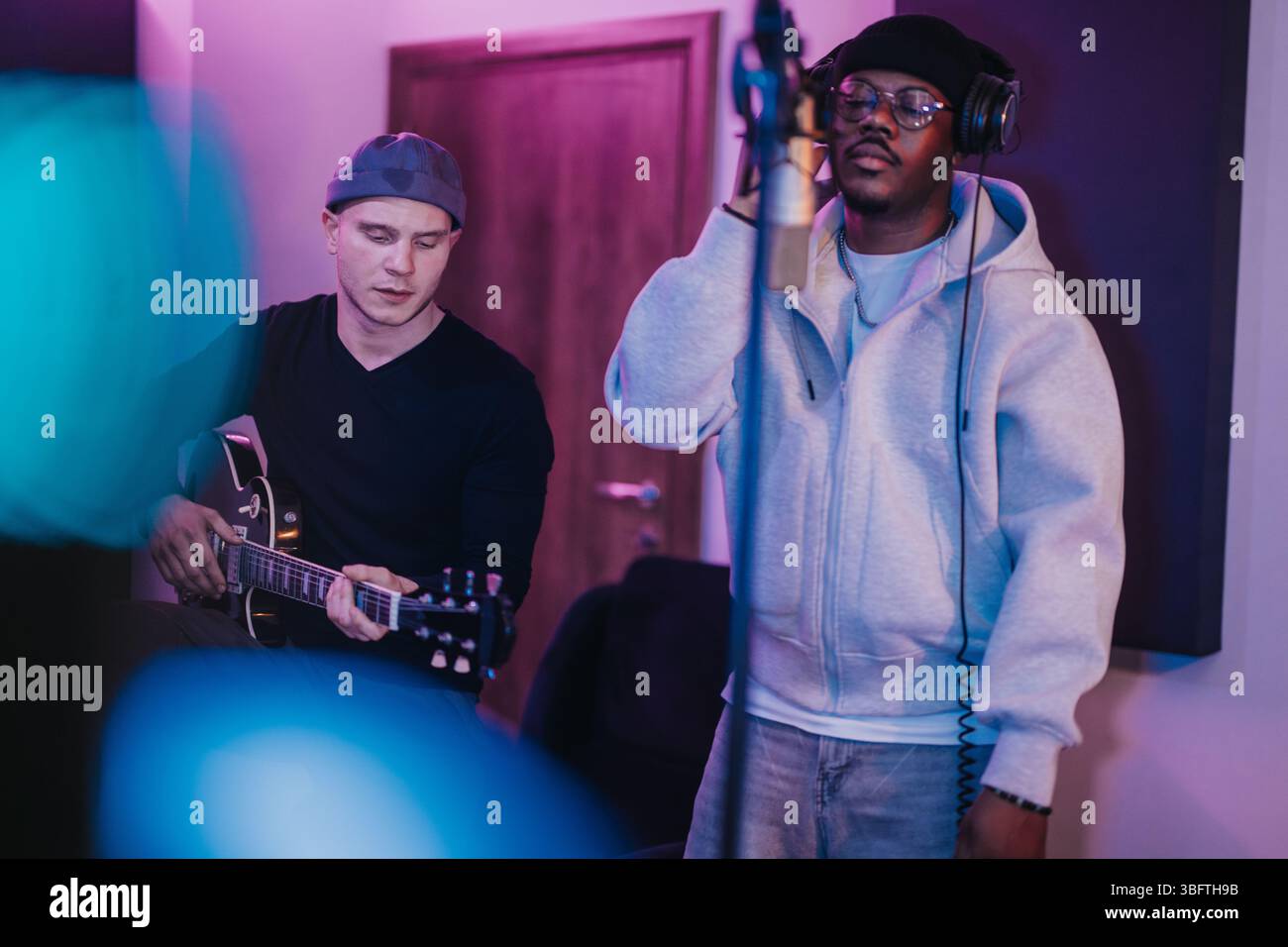 Two musicians are captured in a recording studio setting, one playing ...