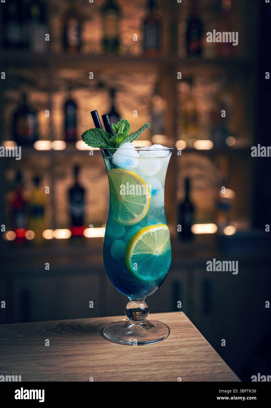 Blue lagoon cocktail standing on bar counter with blurred bottles in ...
