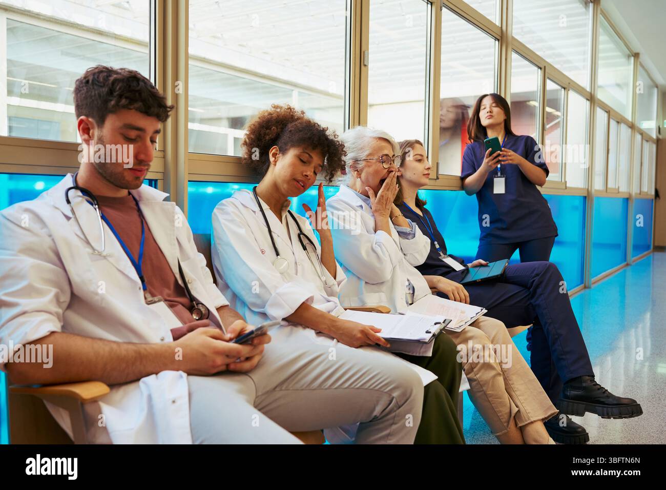 Tired medical team waiting in hospital corridor: doctors and nurses ...