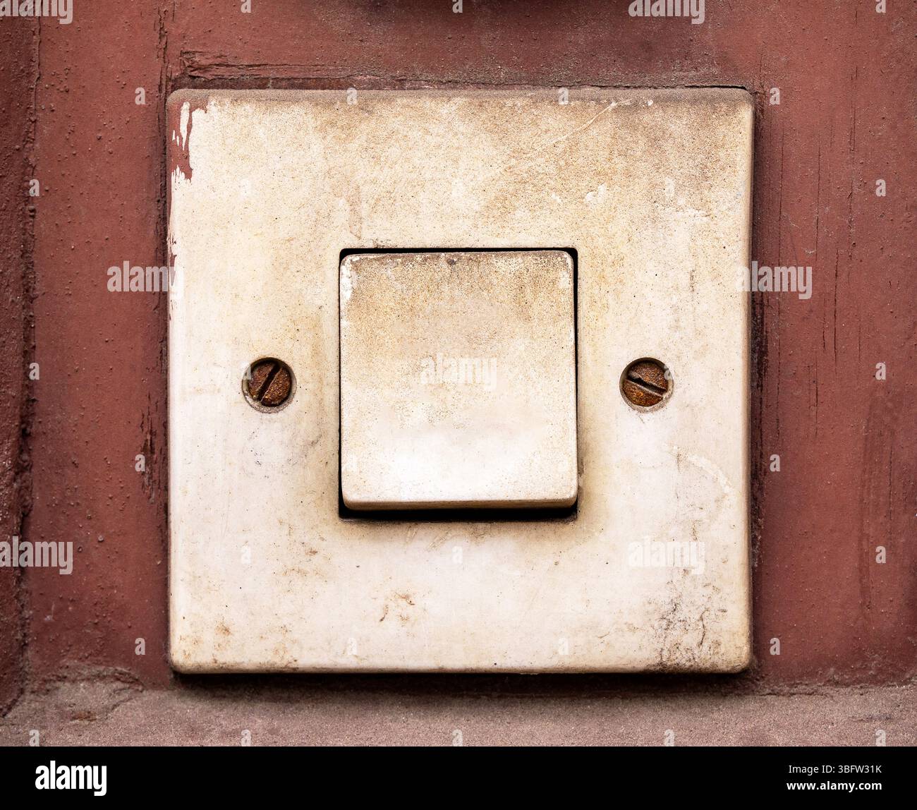 Old dirty electric light switch or doorbell button on a rusty red wall ...