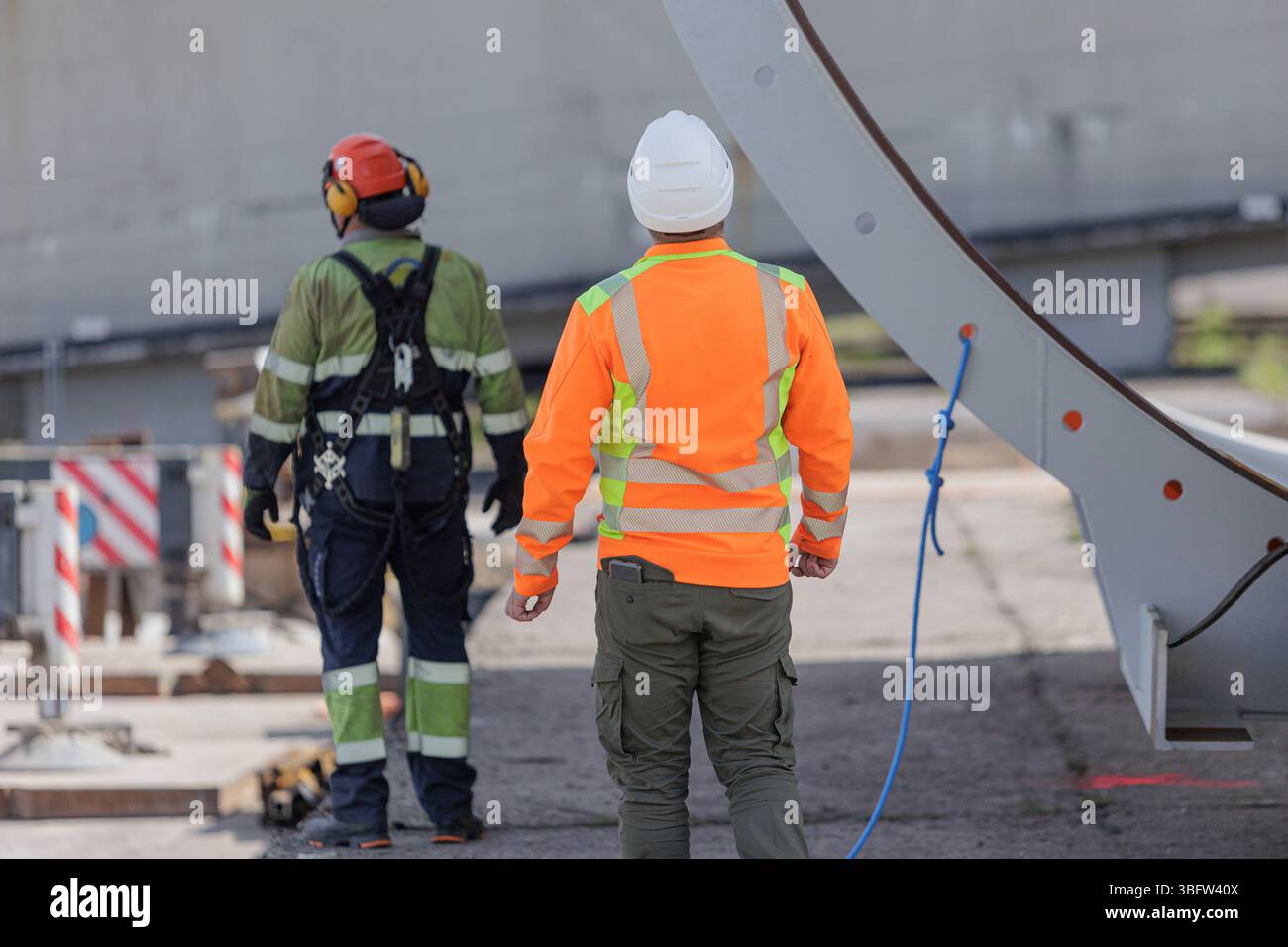 Two construction workers in safety gear monitoring large metal ...