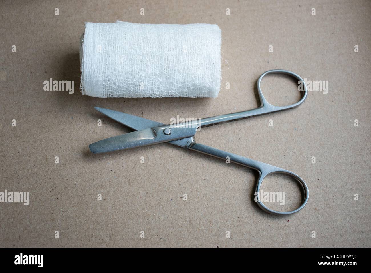 A pair of stainless steel medical scissors placed beside a rolled white ...