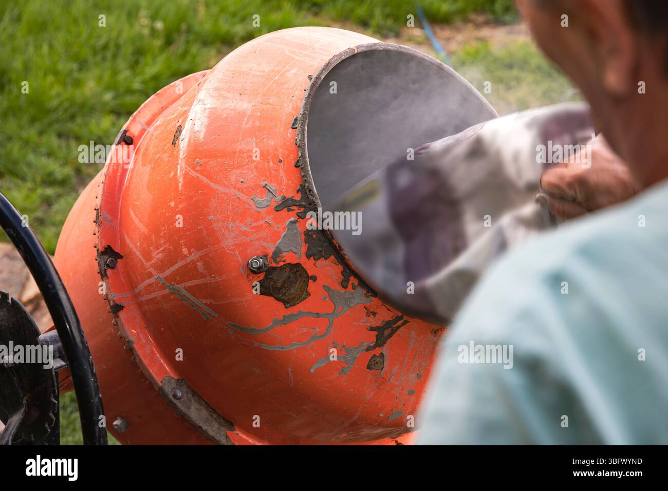 Worker pouring dry cement from bag into orange concrete mixer on ...