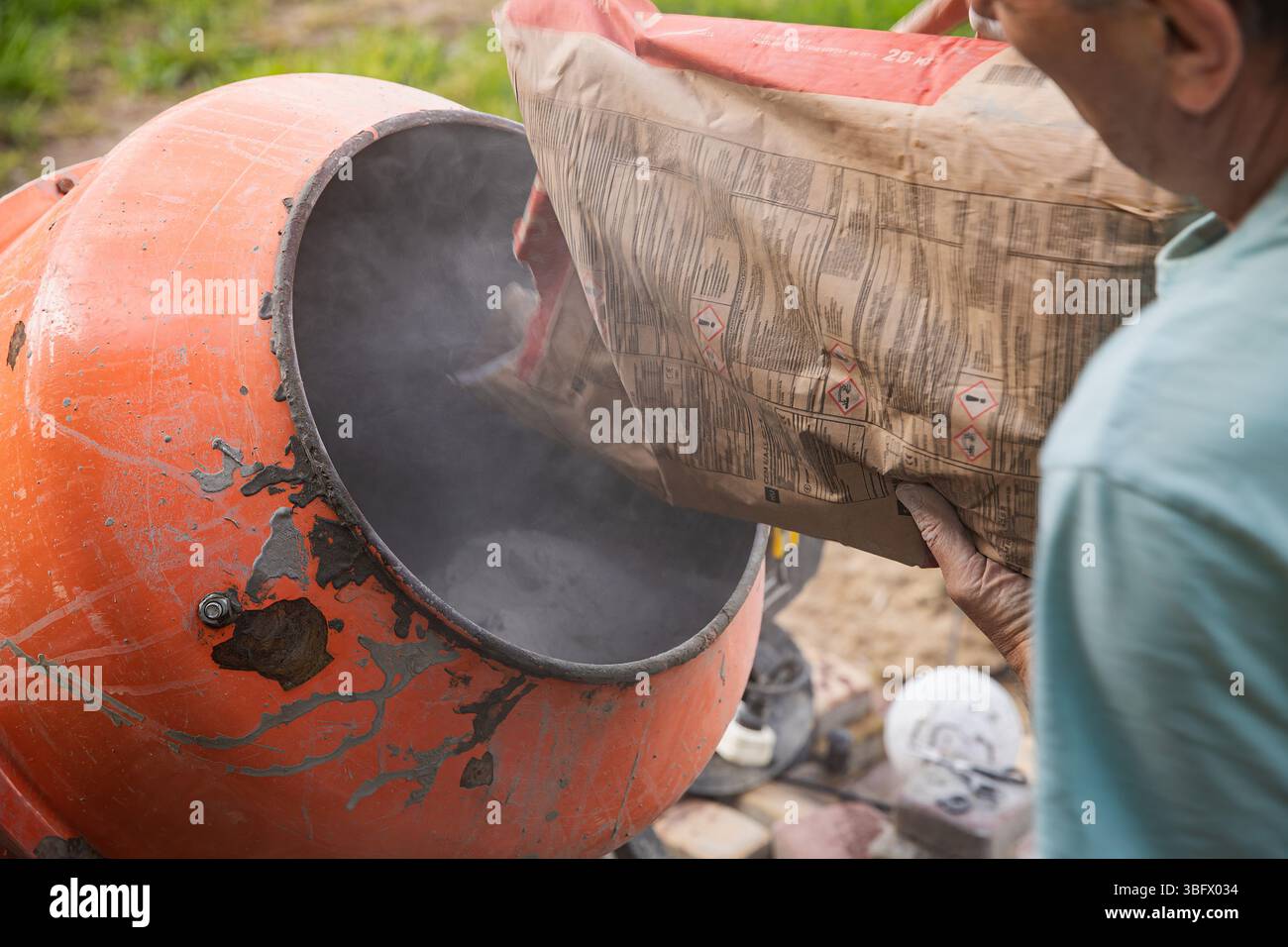 Worker pouring dry cement from bag into orange concrete mixer on ...