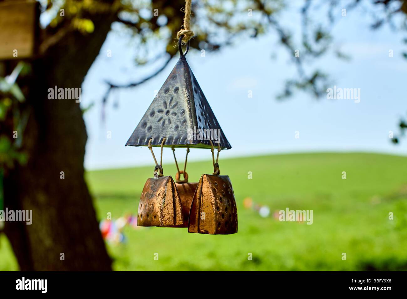 Decorative metal wind chimes hanging from a tree branch, creating a ...