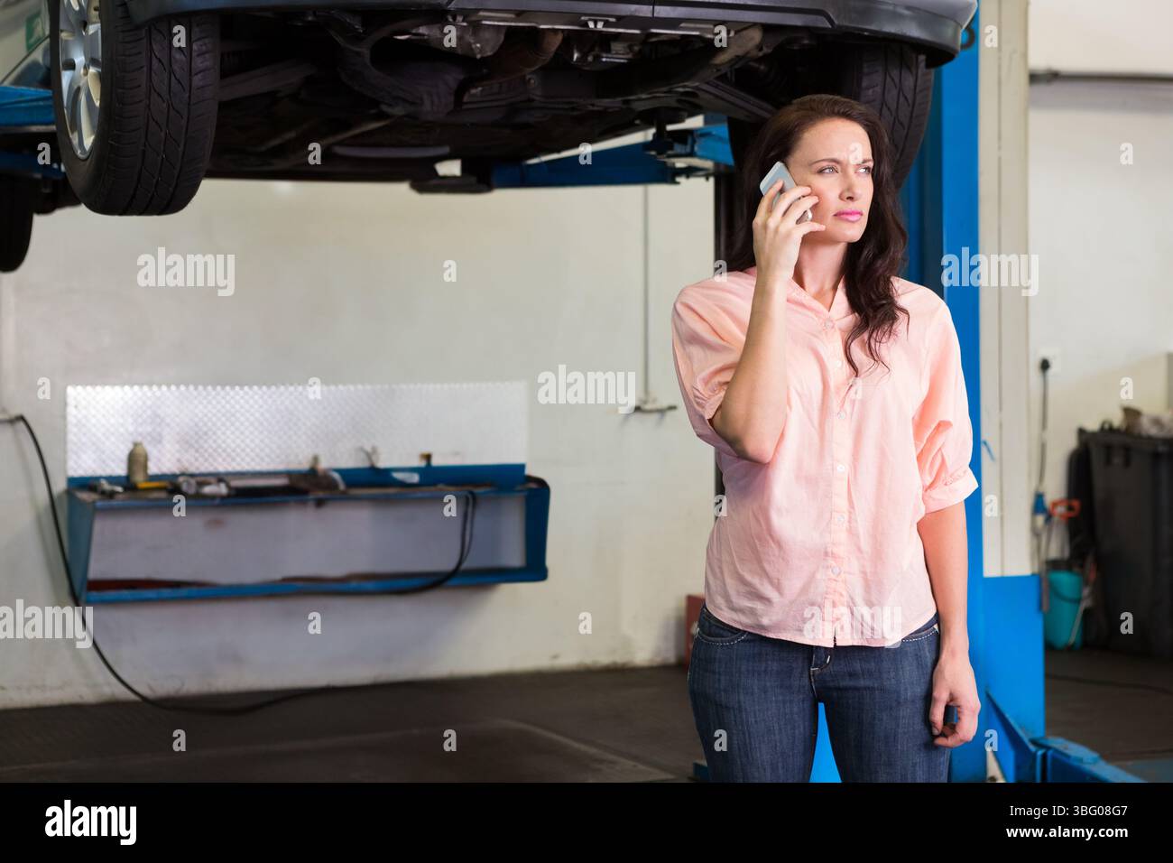 Woman standing in auto garage holding smartphone and examining raised ...