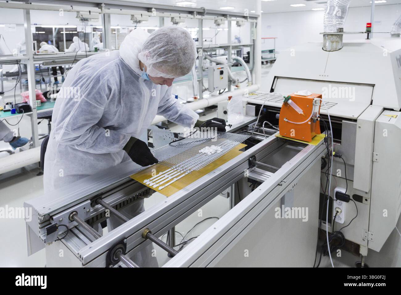 A factory worker in a white lab suit and black latex gloves, working ...