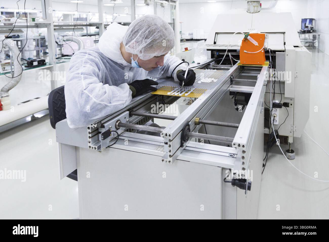 A factory worker in a white lab suit and latex gloves, working with a ...