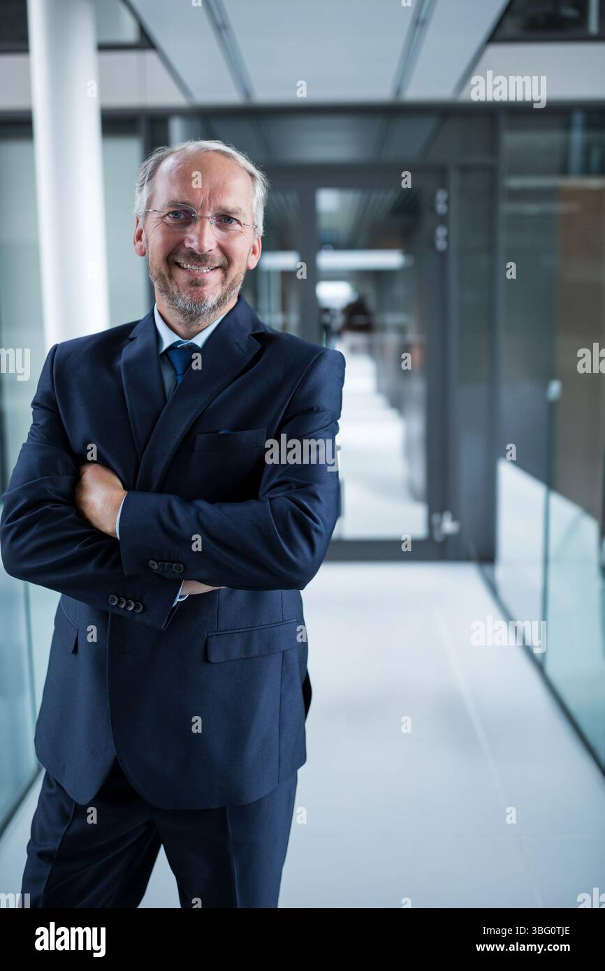 Executive standing wearing eyeglasses with arms crossed in office ...