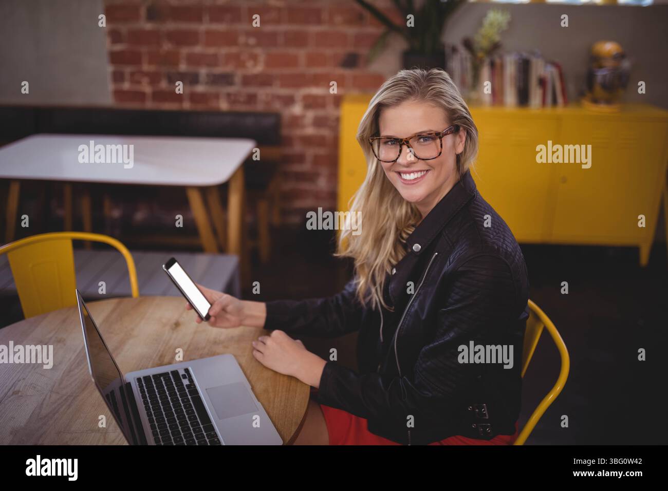 Woman wearing glasses and leather jacket sitting at table in cafe ...